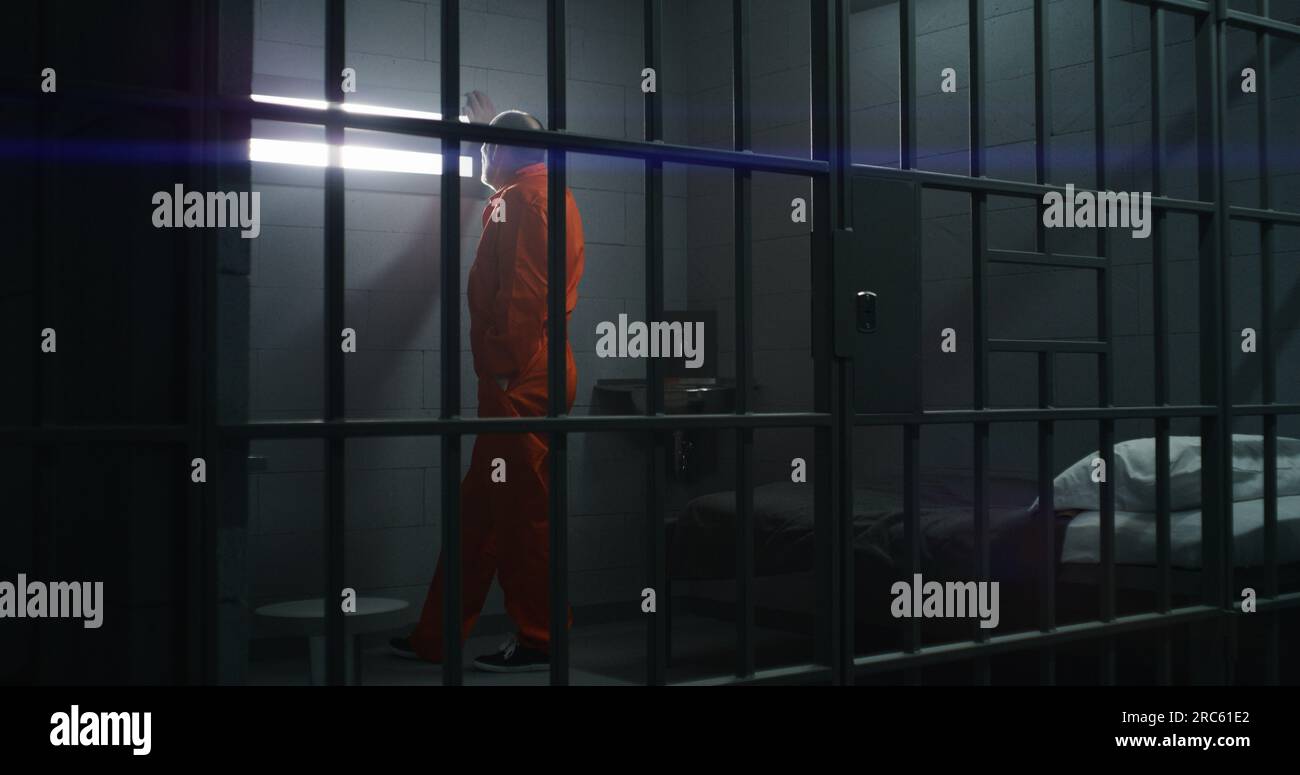 Elderly prisoner in orange uniform leans hands on metal bars. Criminal ...