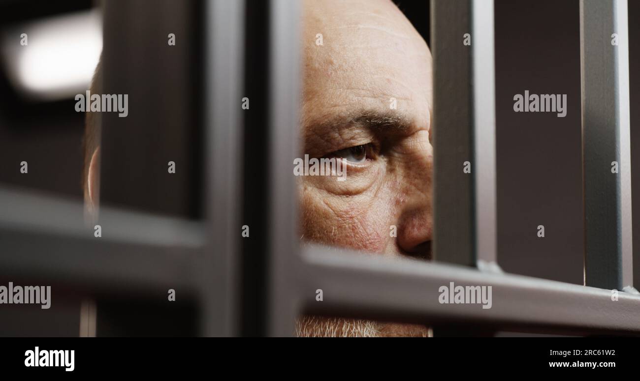 Face close up of depressed elderly prisoner standing behind metal bars ...