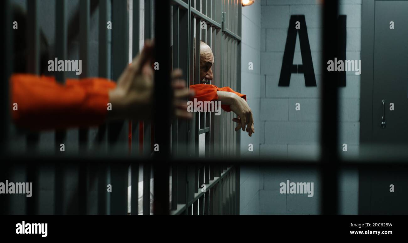 Prisoners in orange uniforms lean on metal bars in prison cells. Guilty ...