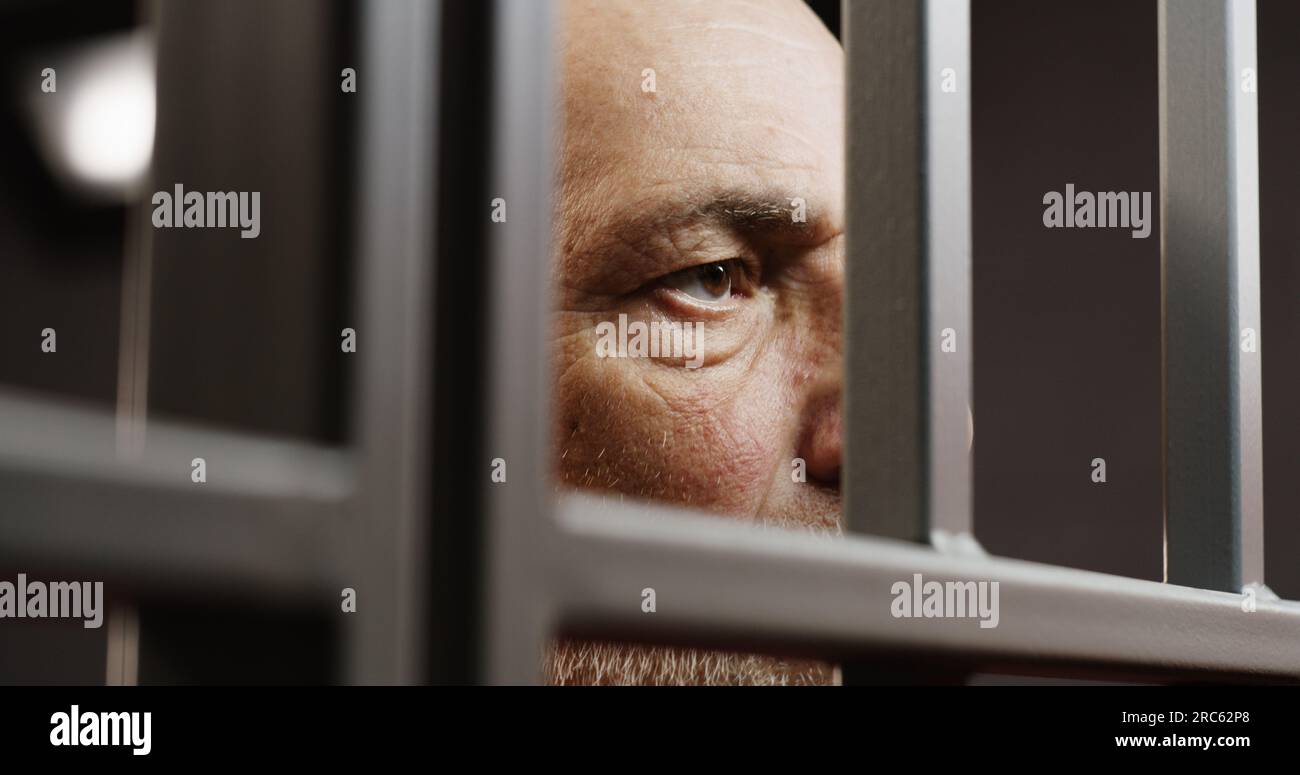Face close up of depressed elderly prisoner standing behind metal bars ...
