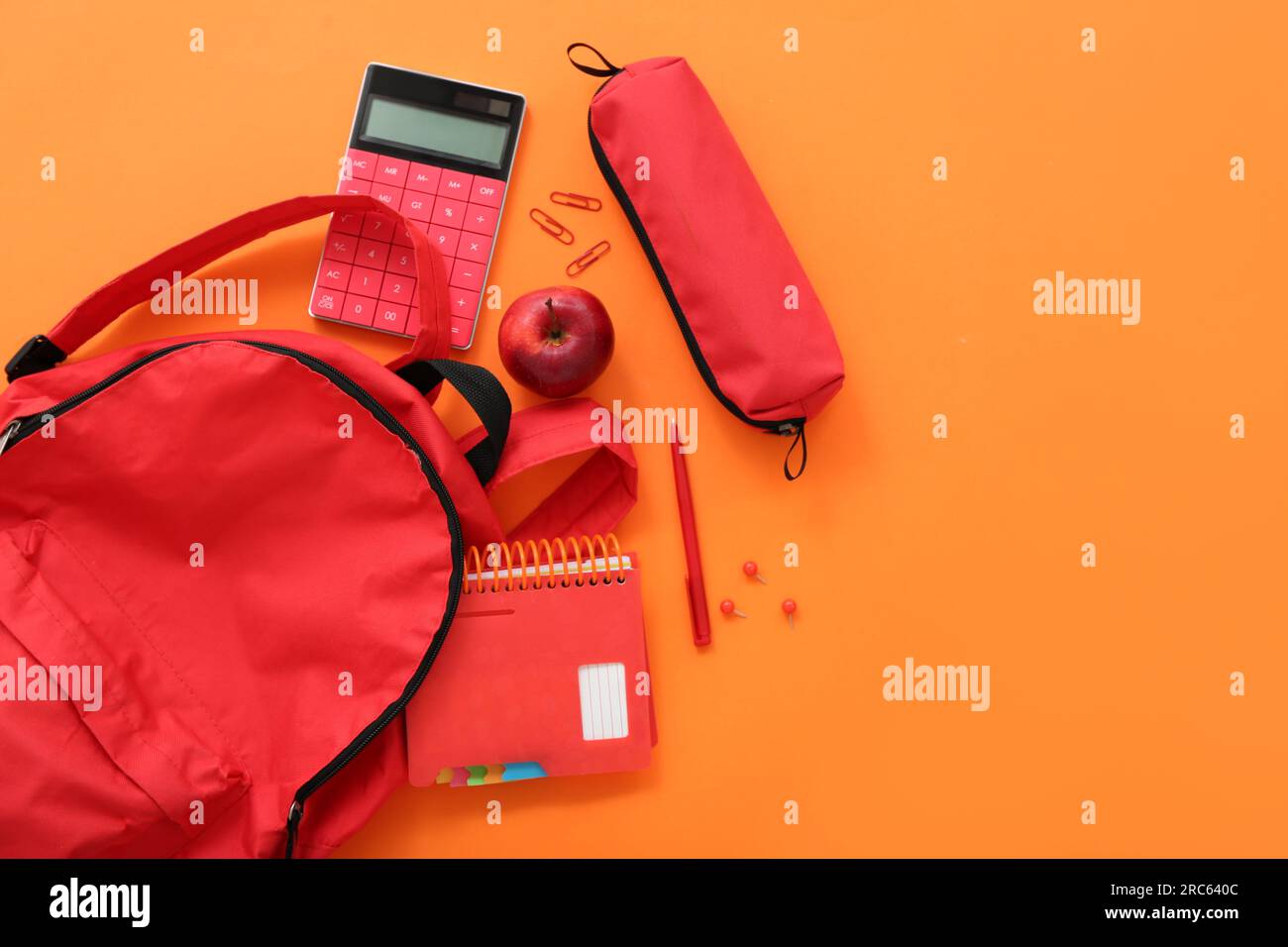 Red school backpack with pencil case, calculator and apple on orange ...