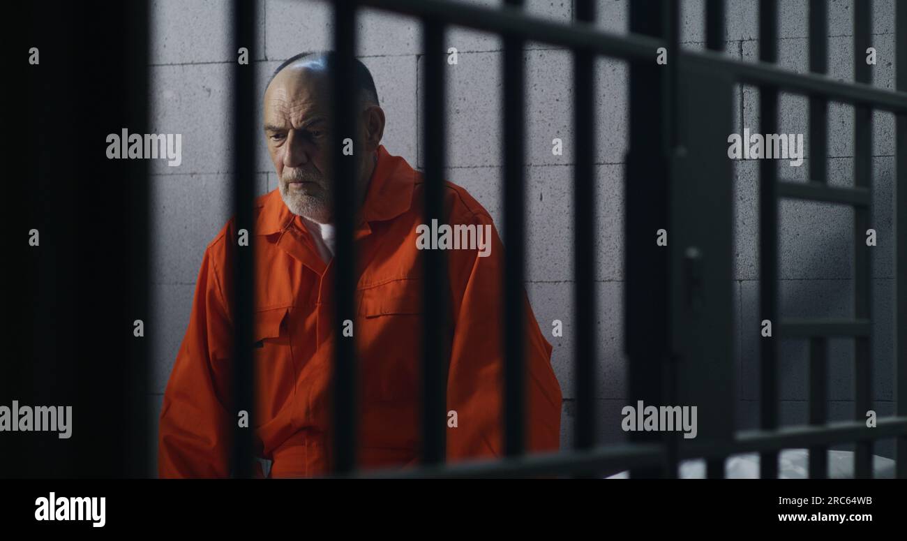 Elderly Criminal In Orange Uniform Sits On Prison Bed And Thinks About