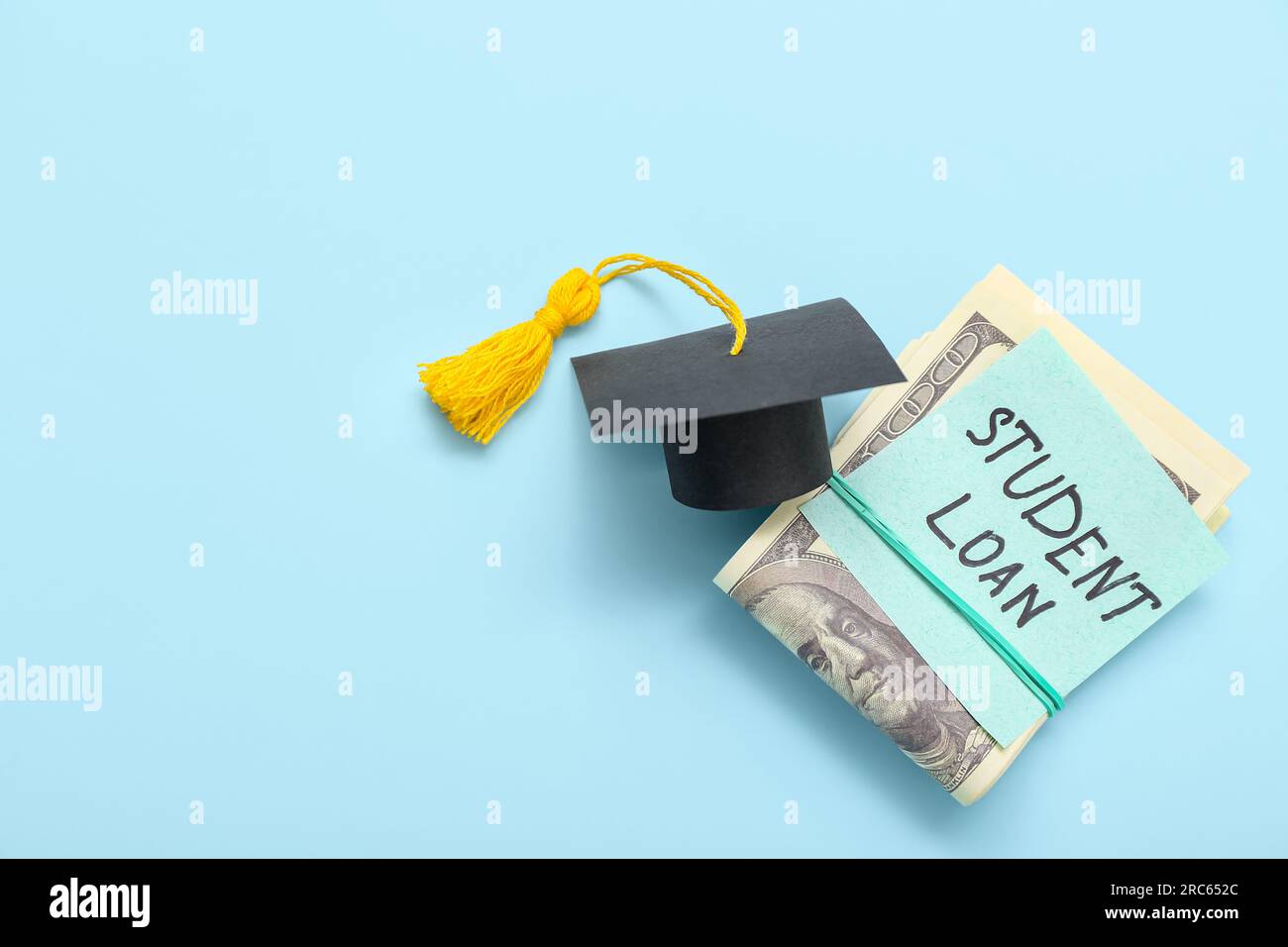 Dollar banknotes, graduation cap and sticky note with text STUDENT LOAN ...