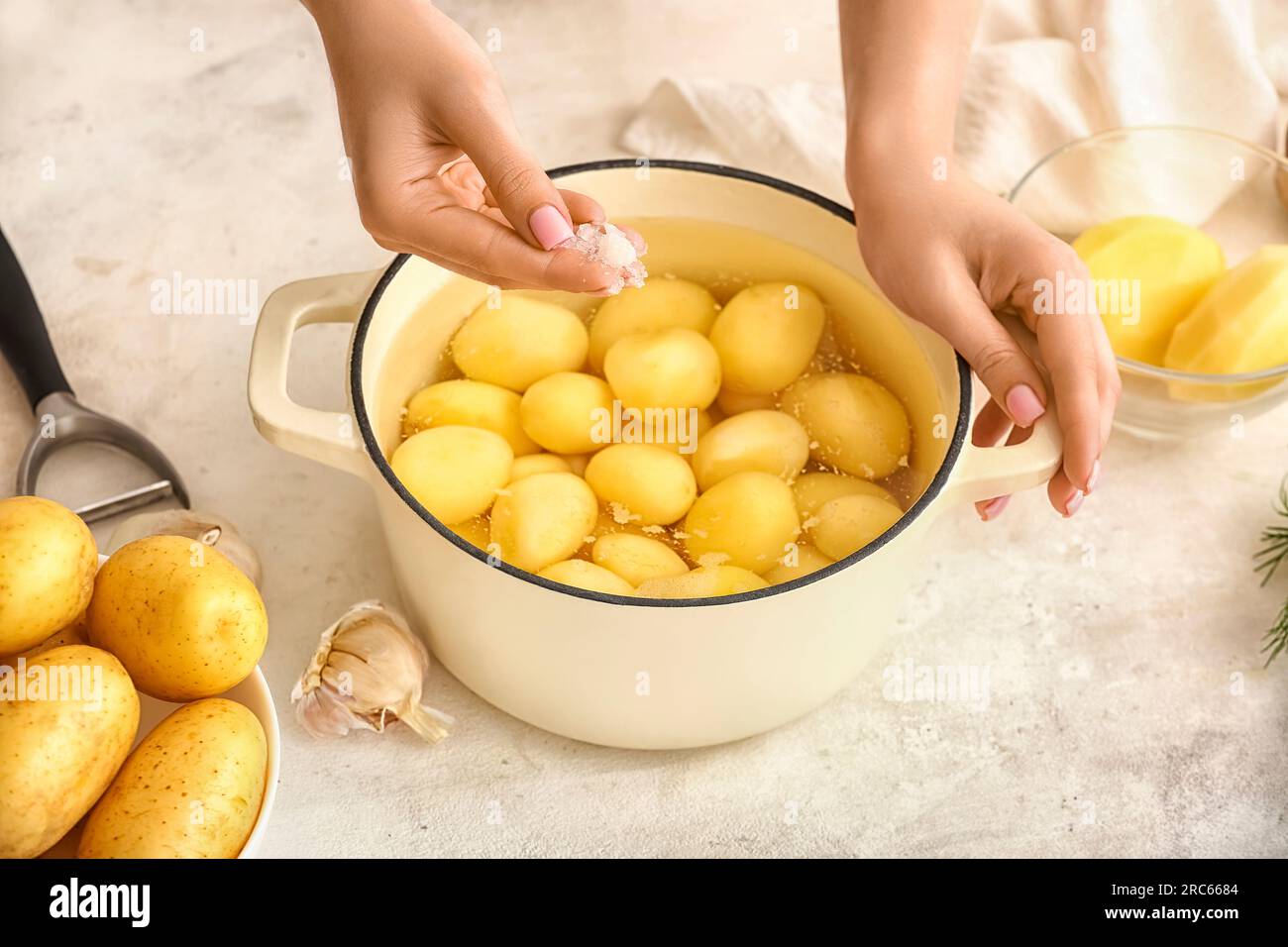 Woman adding salt into pot with peeled potatoes on light background ...
