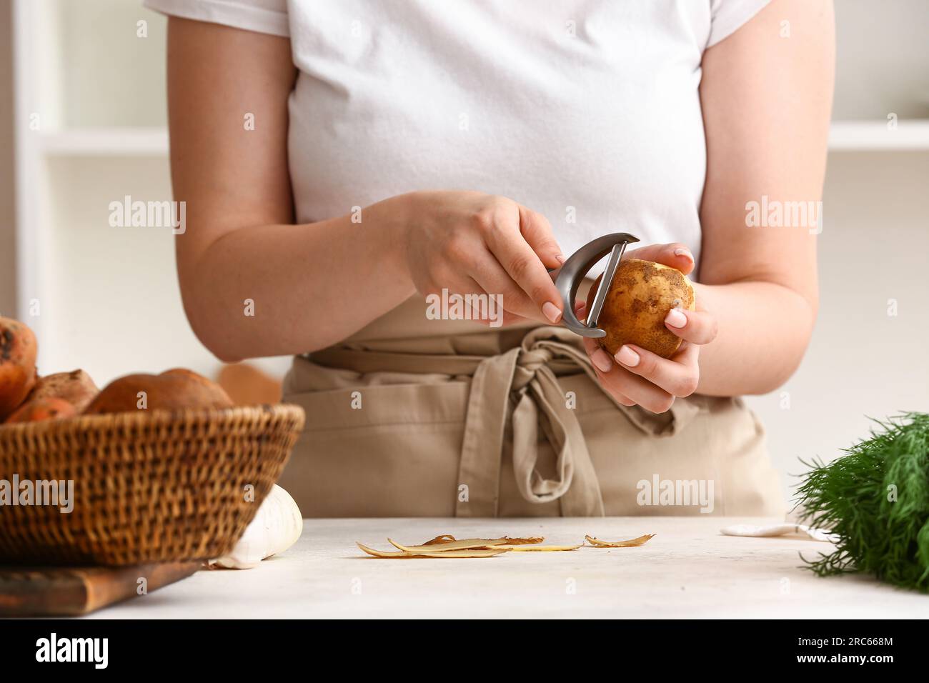 Woman peeling raw potato at table in kitchen Stock Photo - Alamy