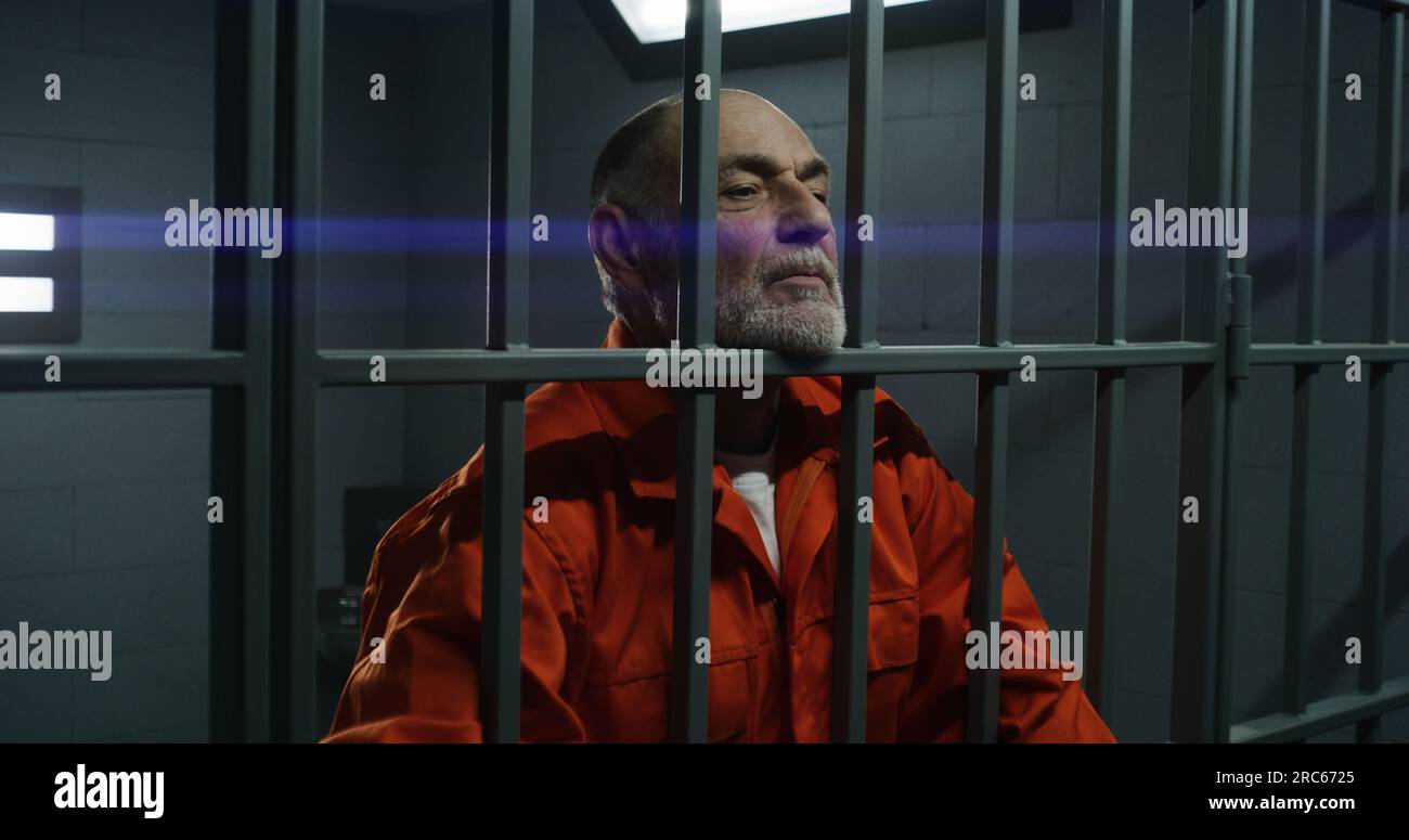 Elderly prisoner in orange uniform stretches fingers, leans on metal ...