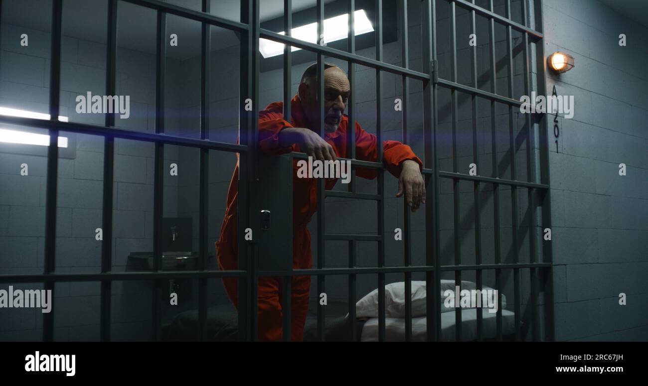 Elderly prisoner in orange uniform leans hands on metal bars. Criminal ...