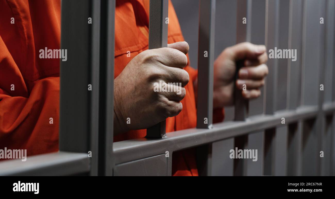 Hands close up of elderly prisoner in orange uniform holding metal bars ...