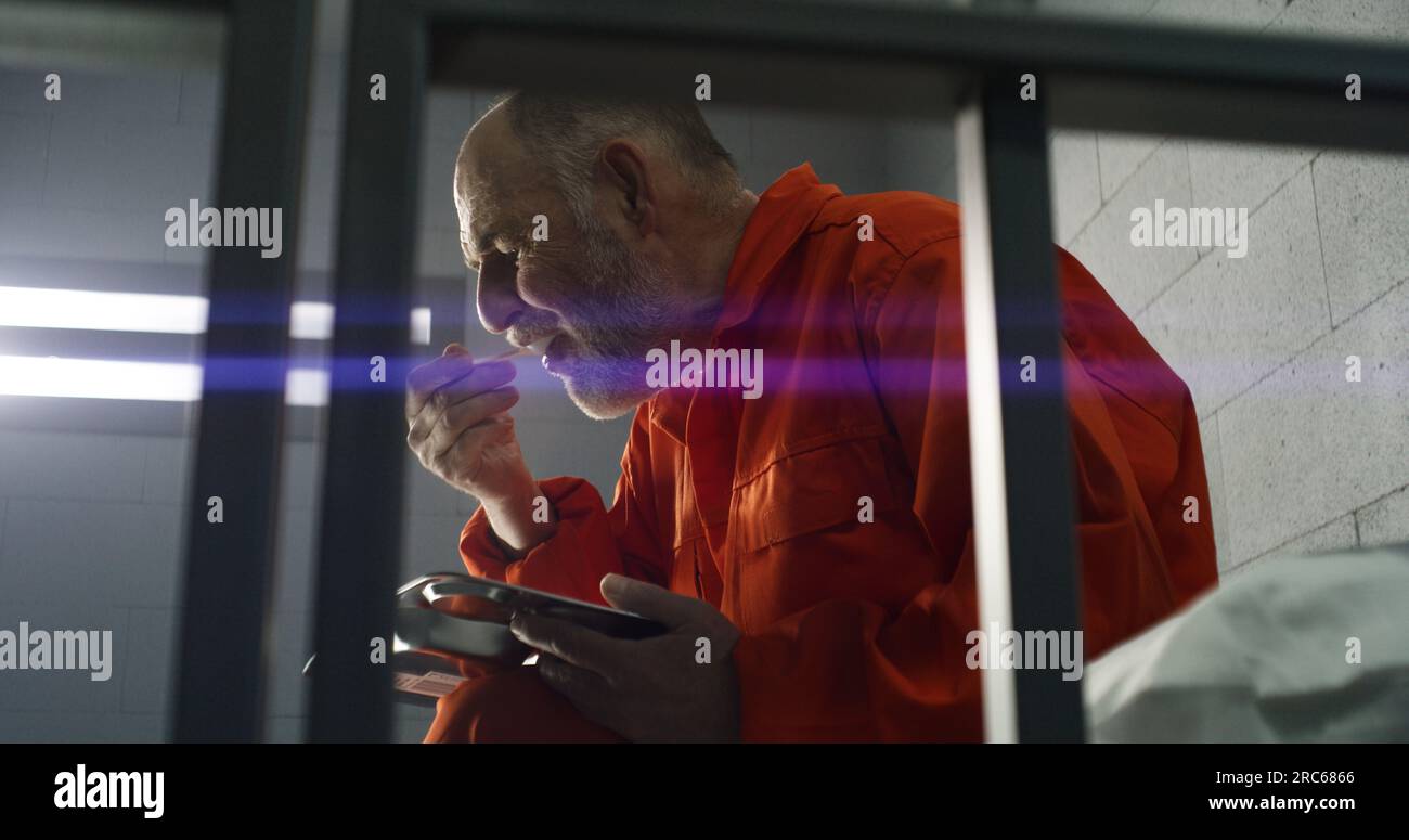 Elderly prisoner, criminal in orange uniform eats dinner sitting in ...