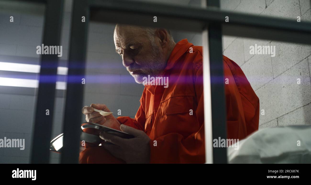Elderly prisoner, criminal in orange uniform eats dinner sitting in ...
