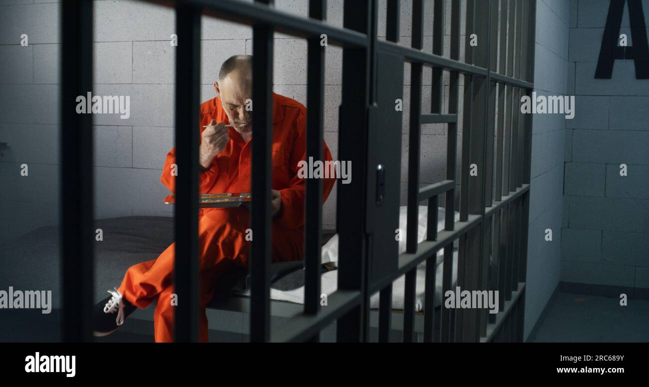 Elderly prisoner, inmate in orange uniform eats food sitting in prison ...