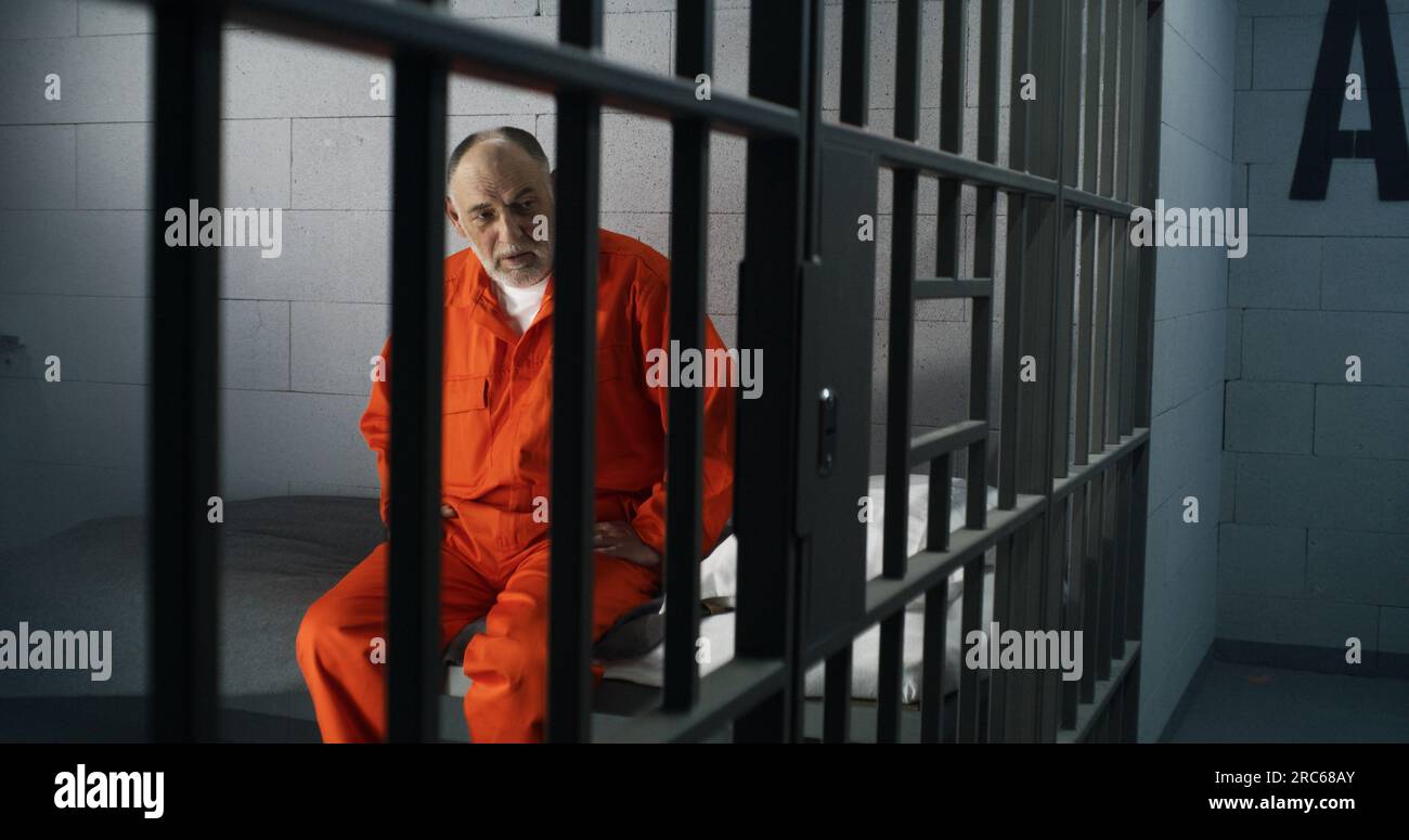 Elderly criminal in orange uniform sits on prison bed and thinks about ...