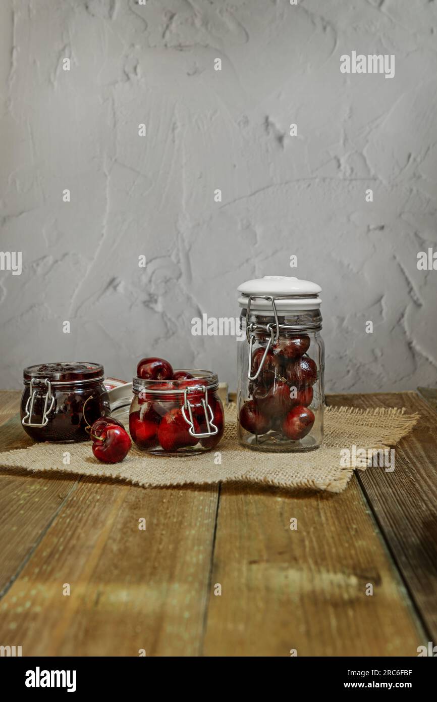 some ripe cherries in transparent glass jars, red frothy jam on an ...