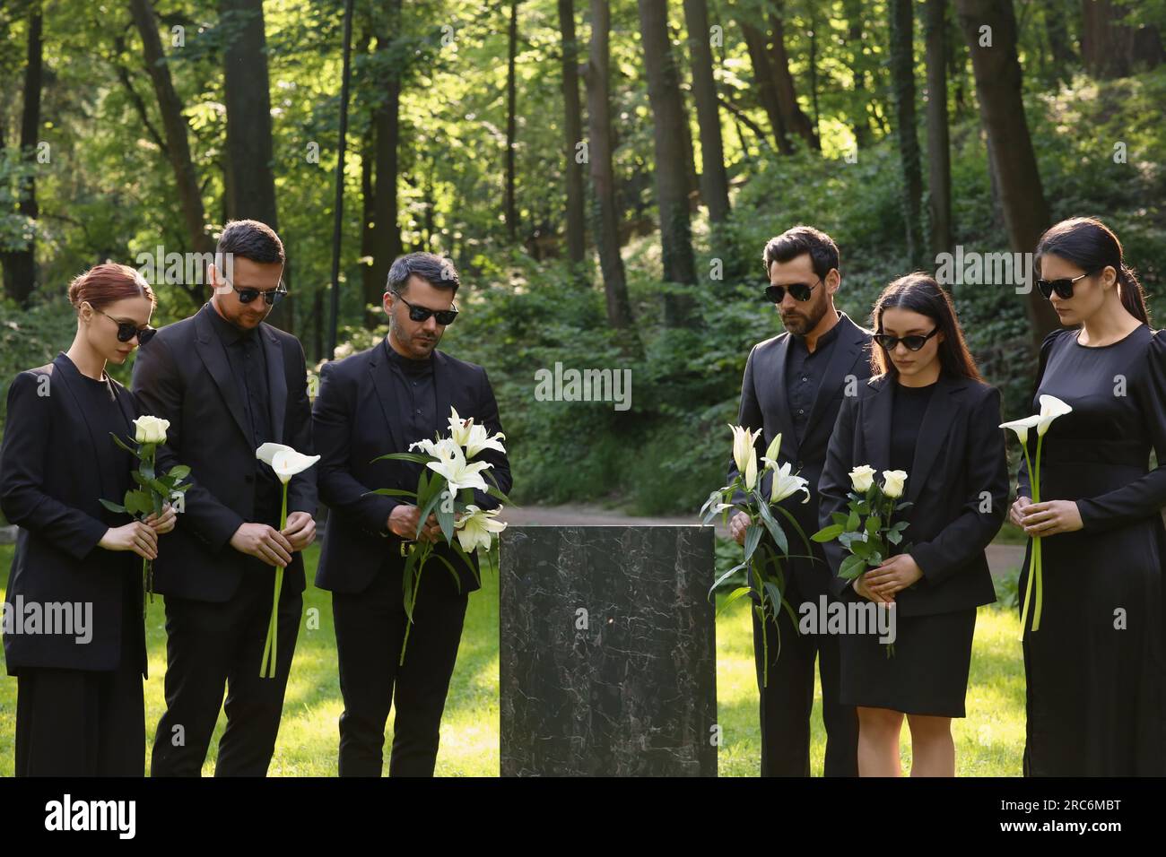 Sad people with flowers mourning near granite tombstone at cemetery ...