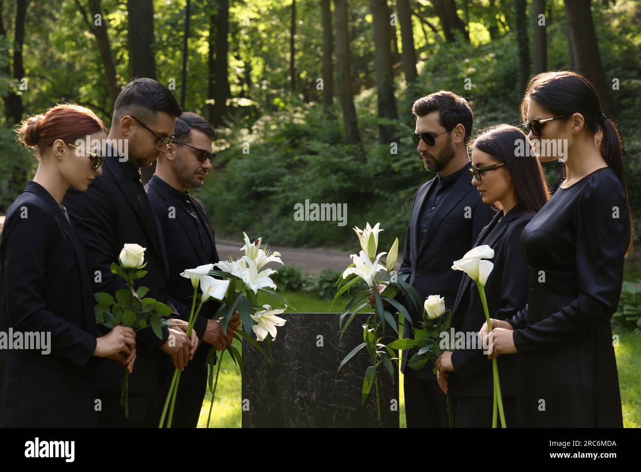 Sad people with flowers mourning near granite tombstone at cemetery ...