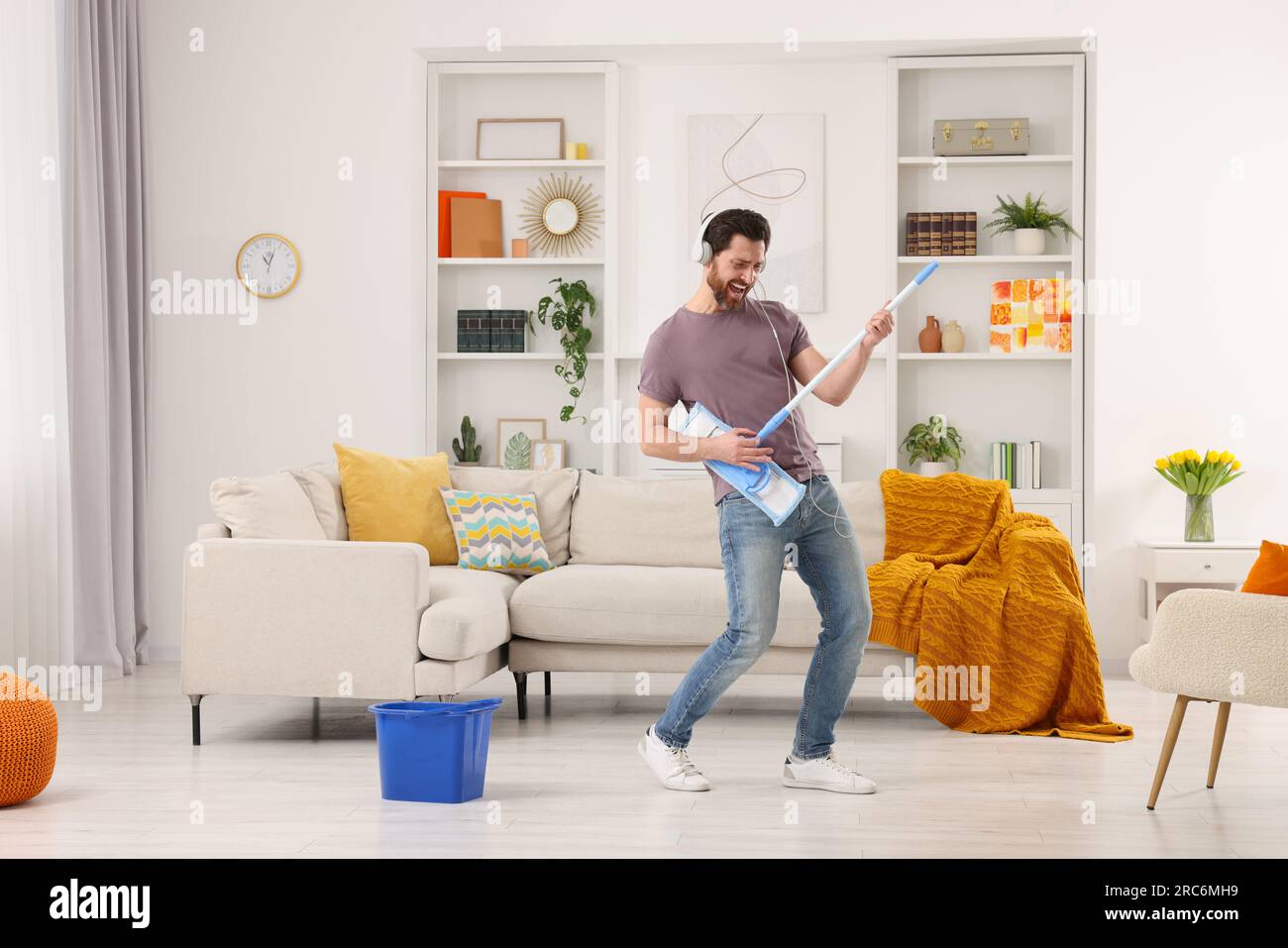 Spring cleaning. Man in headphones with mop singing while tidying up ...