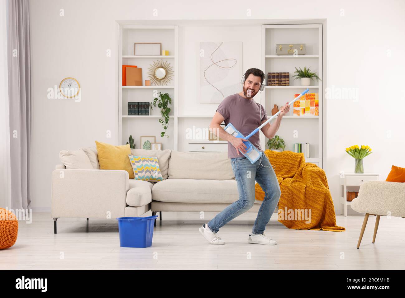Spring cleaning. Man in headphones with mop singing while tidying up ...
