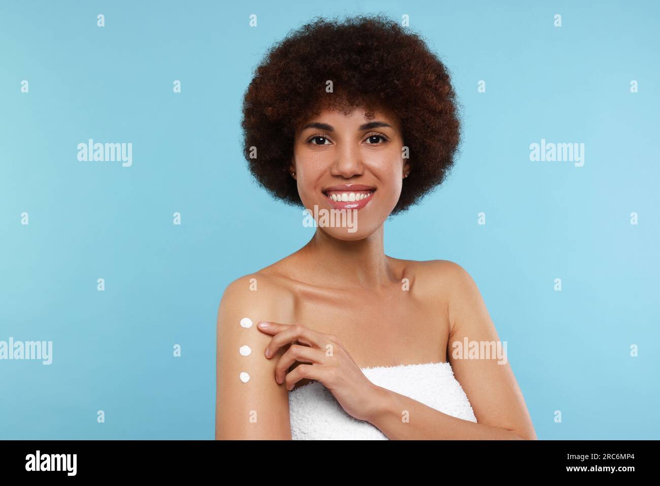 Beautiful young woman applying body cream onto arm on light blue ...
