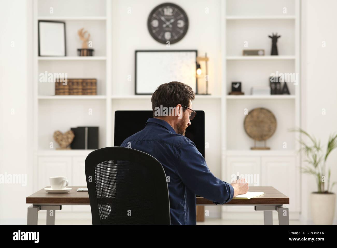 Home workplace. Man working at wooden desk in room, back view Stock ...