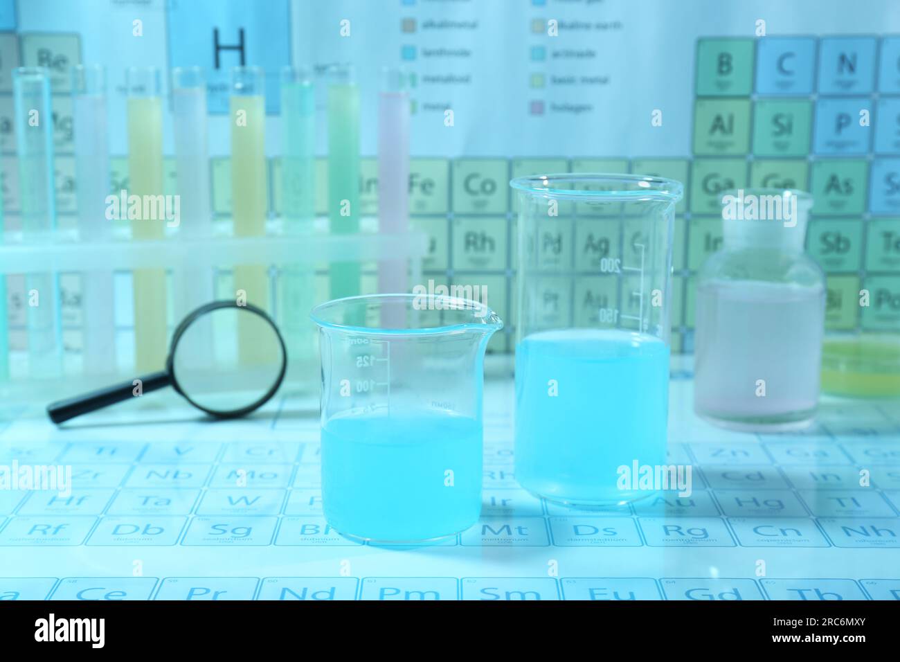 Different laboratory glassware with liquids and magnifying glass on ...