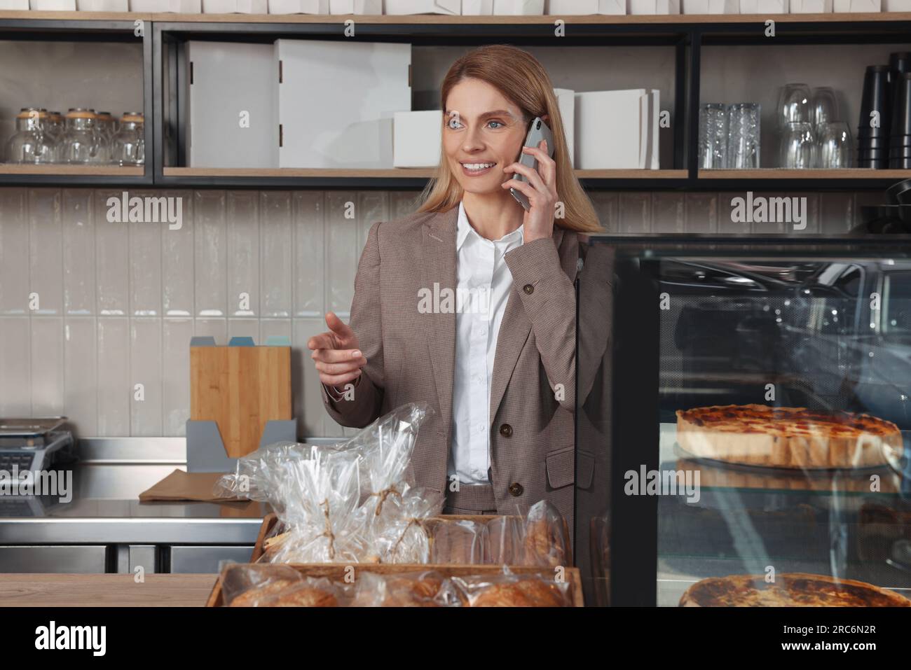 Happy business owner talking on phone at cashier desk in bakery shop ...