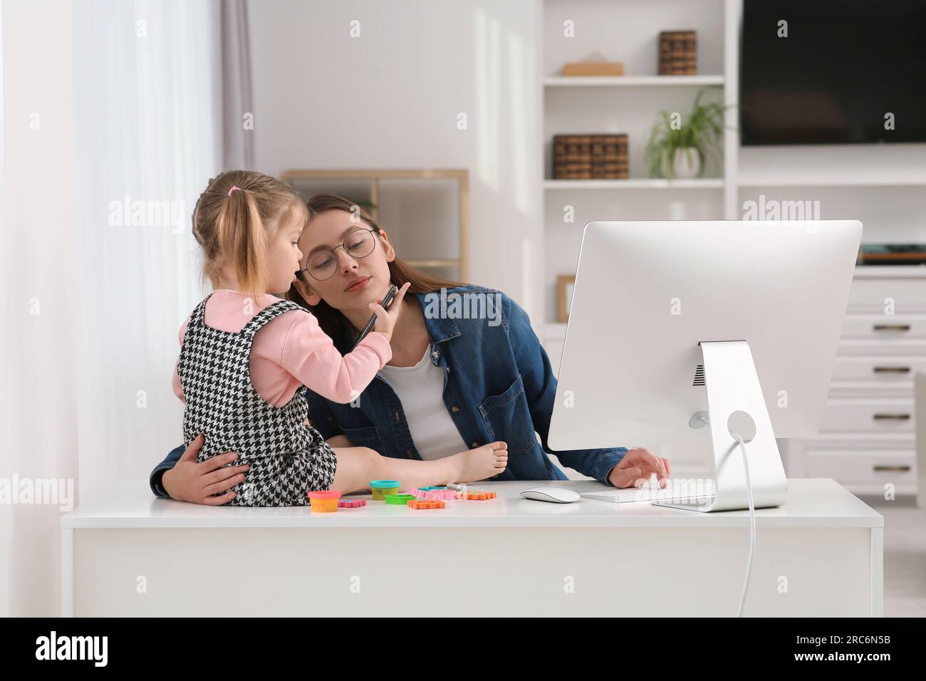 Mother spending time with her daughter at home. Child sitting on desk ...