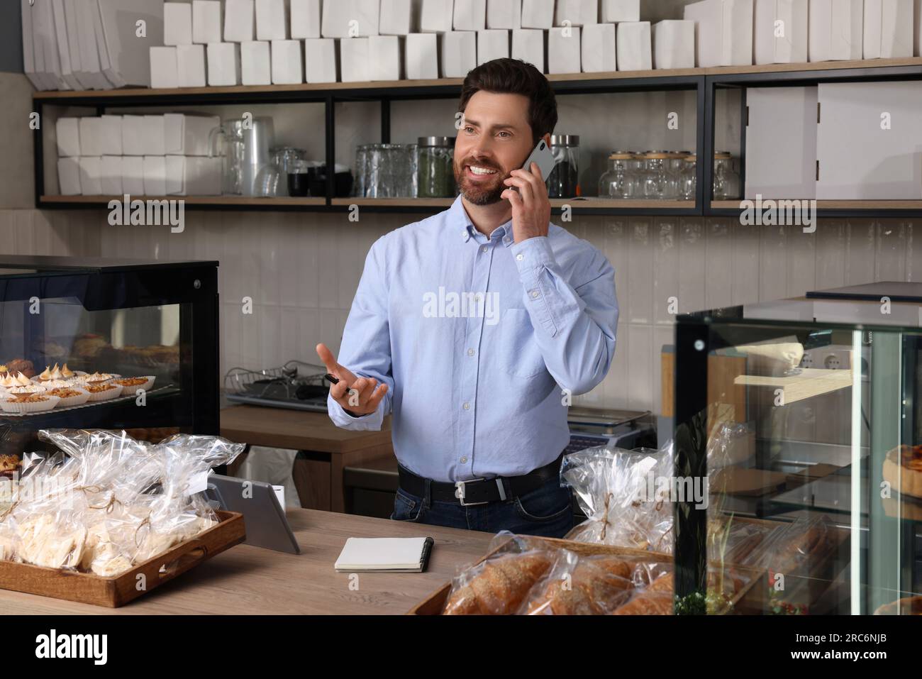 Happy business owner talking on phone at cashier desk in bakery shop ...