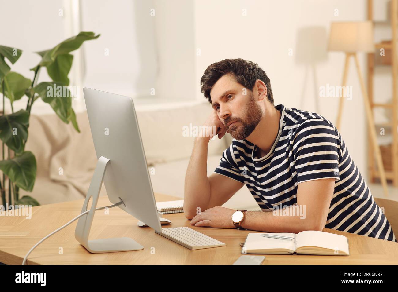 Home workplace. Tired man working with computer at wooden desk in room ...