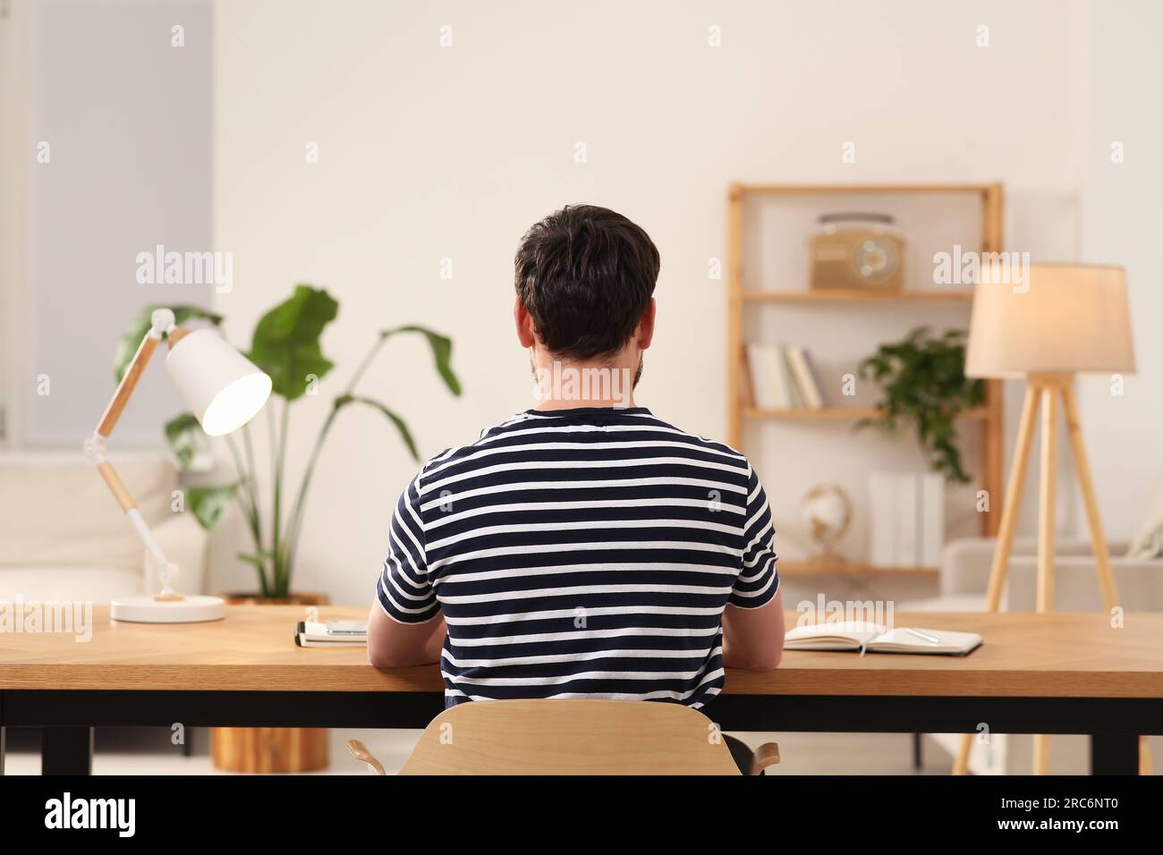 Home workplace. Man working at wooden desk in room, back view Stock ...