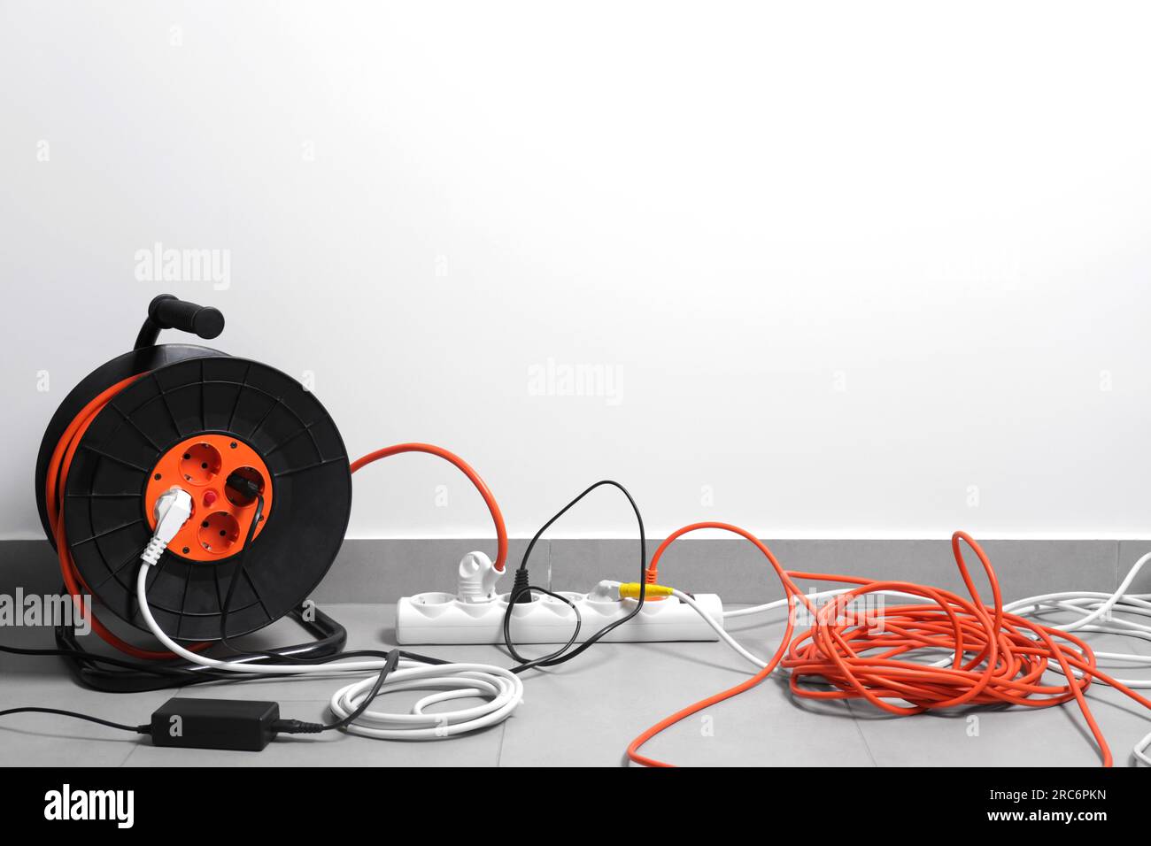 Extension cord reel plugged into power strip on grey floor indoors ...