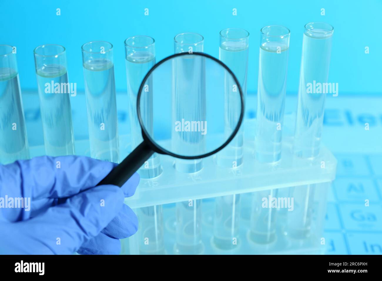 Scientist with magnifying glass examining test tubes in laboratory ...