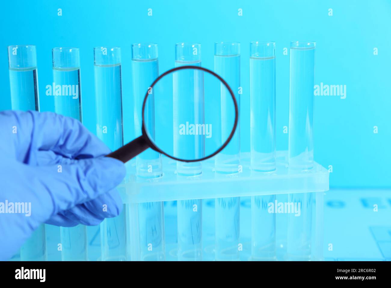 Scientist with magnifying glass examining test tubes in laboratory ...