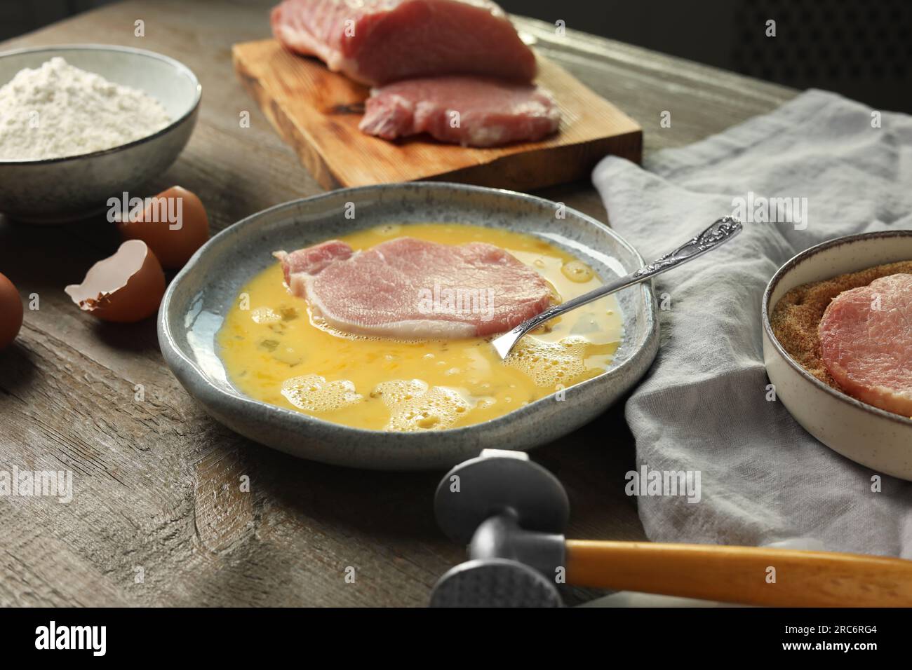 Cooking schnitzel. Raw pork chop in eggs, meat mallet and ingredients ...