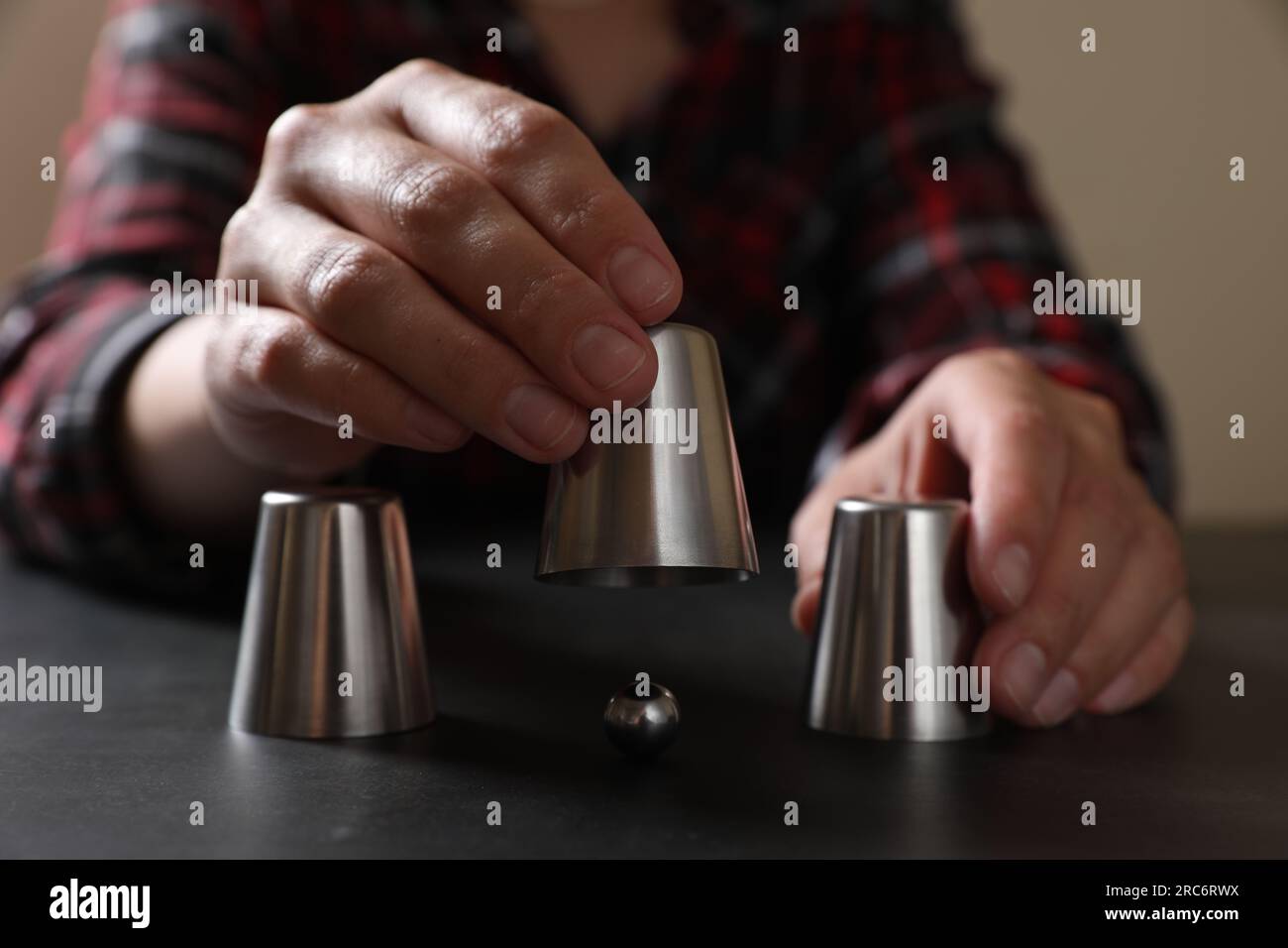 Woman playing thimblerig game with cups and metal ball at black table ...