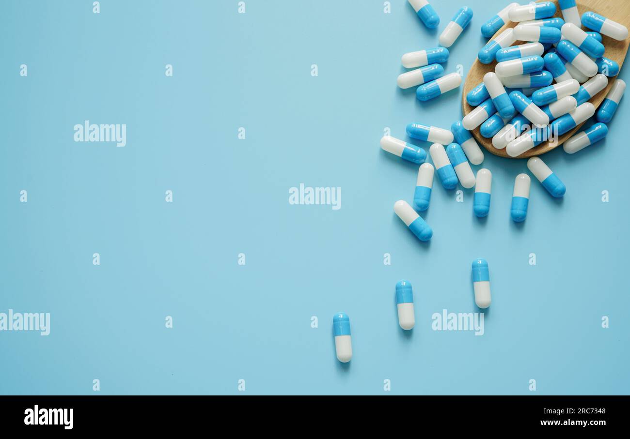 Blue and white antibiotic capsule pill and wooden spoon on blue ...