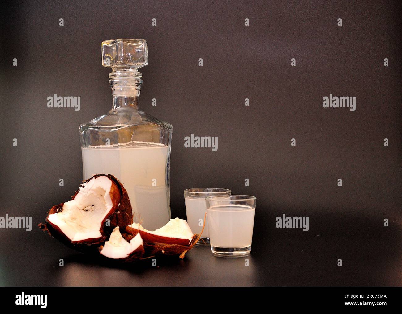 Coconut liqueur and a broken ripe nut on a black background, next to ...
