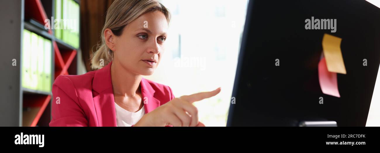 Business woman with serious face at office desk points her finger at ...