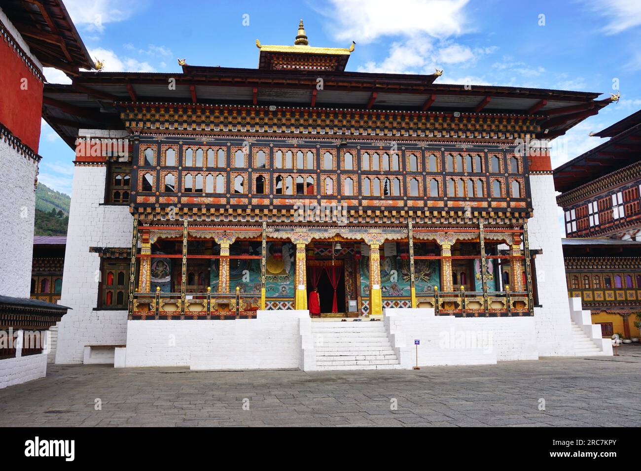 A lone red-robed Buddhist monk stands near the doorway of Dechencholing ...