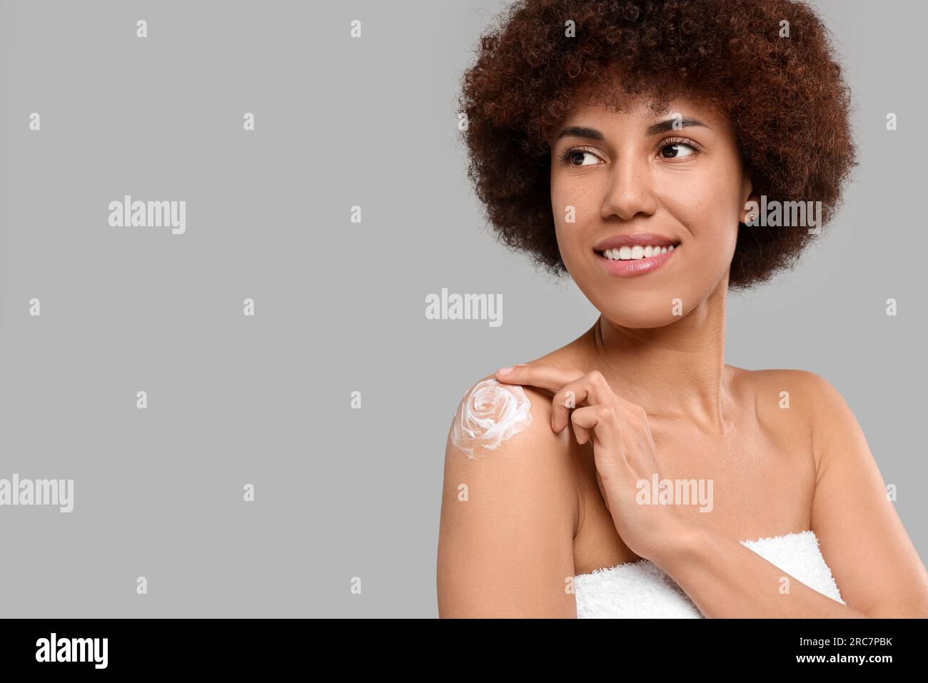 Beautiful young woman applying body cream onto shoulder on grey ...