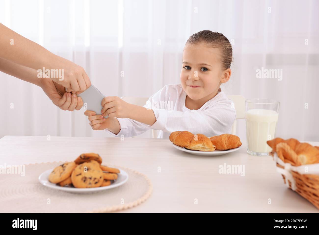 Woman taking away smartphone from her daughter at table indoors ...