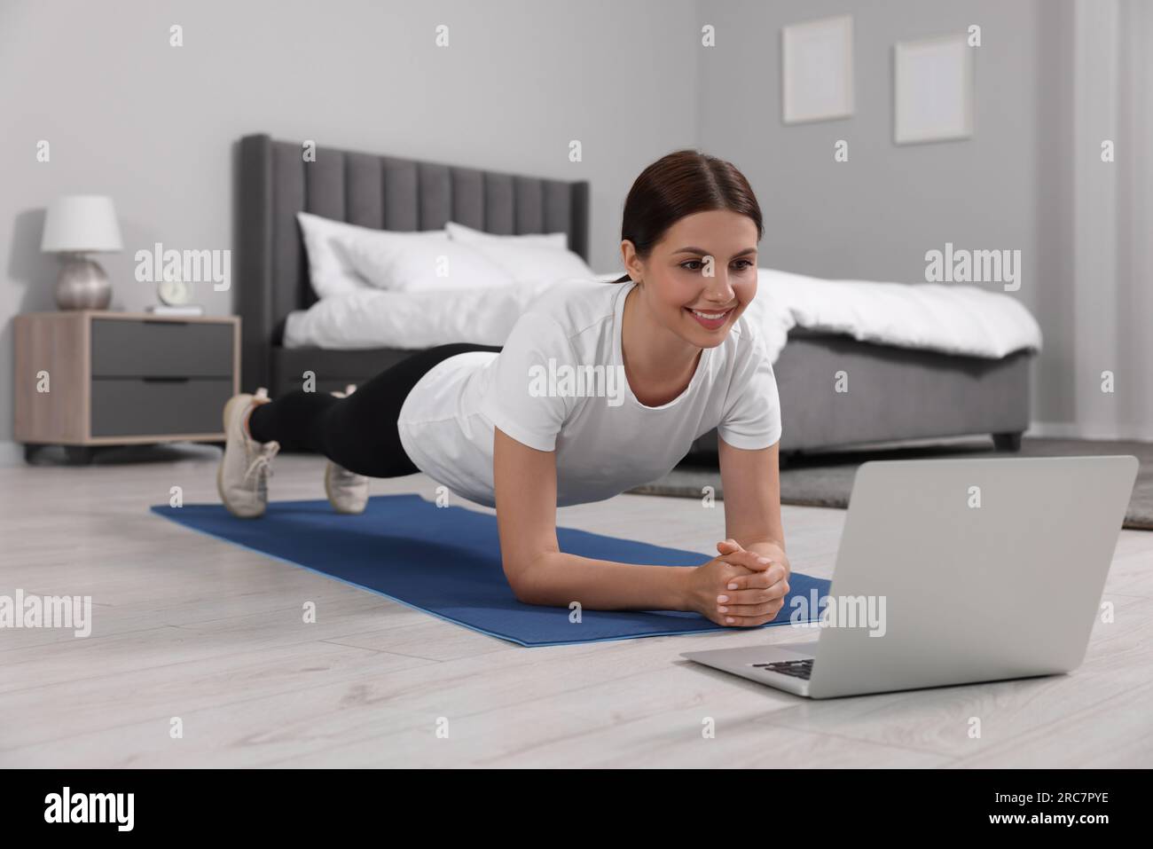 Happy woman doing plank exercise and watching video tutorial via laptop ...