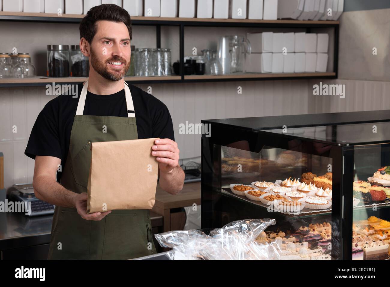 Happy seller with paper bag at cashier desk in bakery shop Stock Photo ...