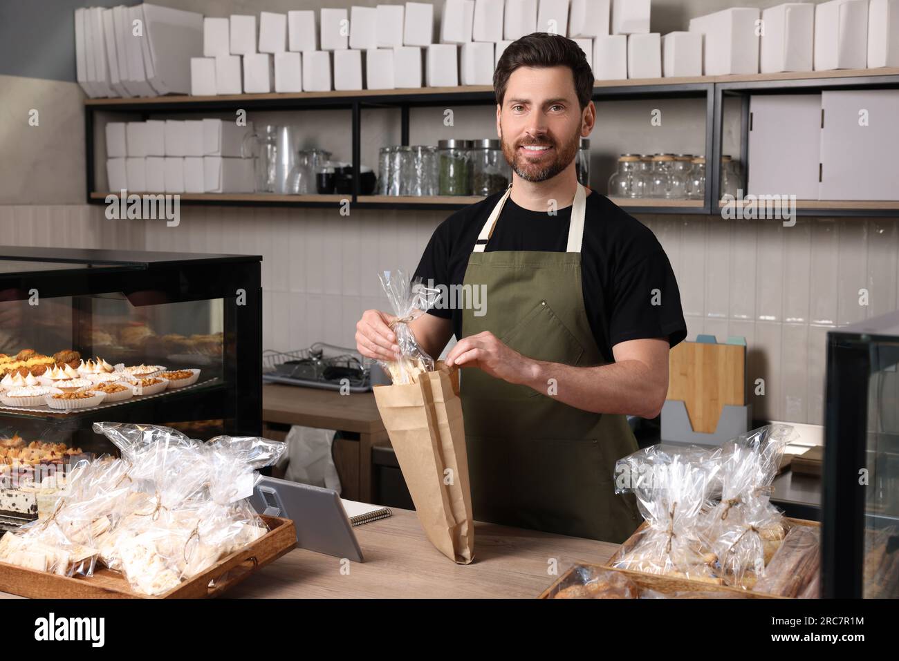 Happy seller putting pastry into paper bag at cashier desk in bakery ...