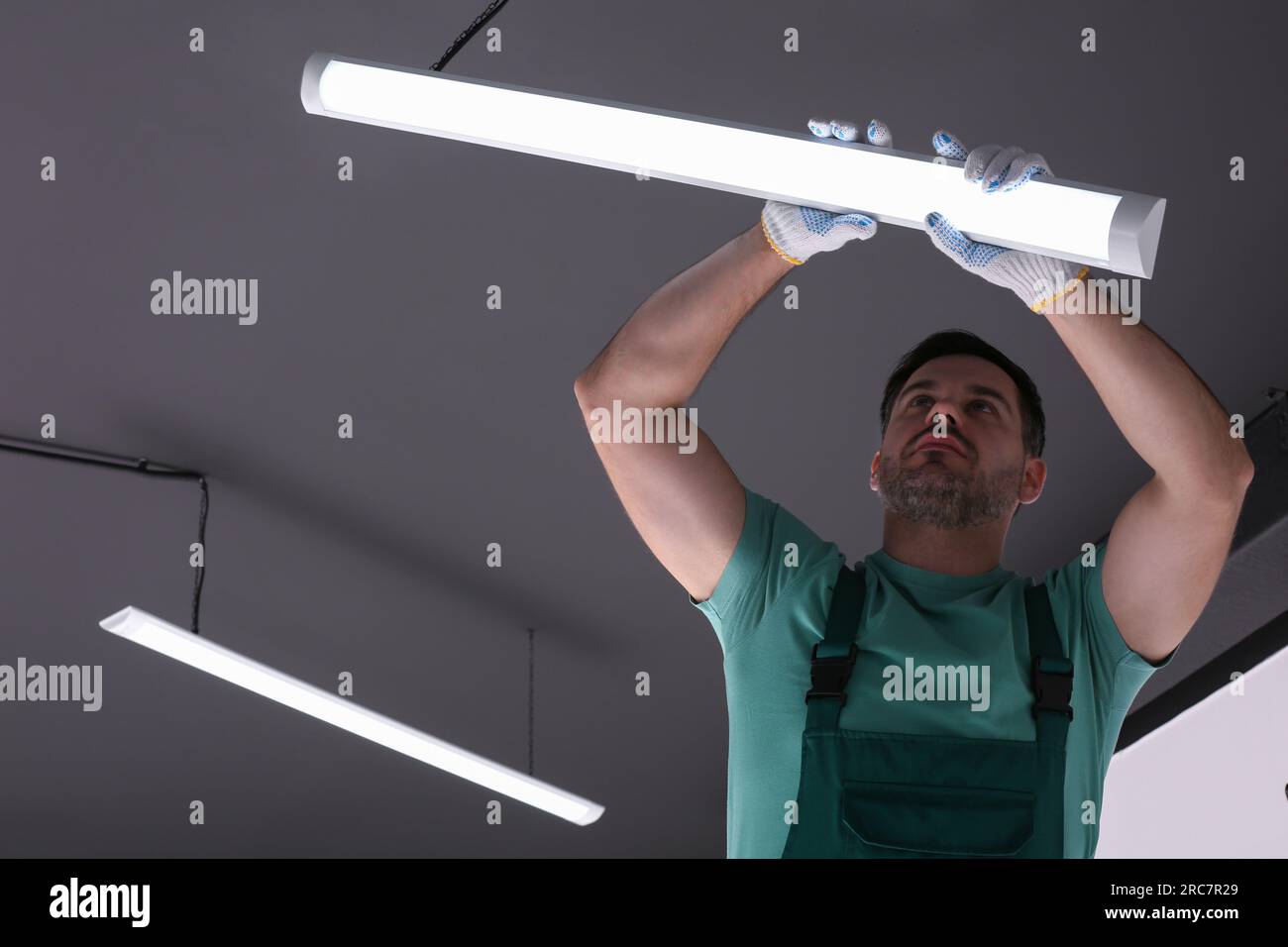 Ceiling light. Electrician installing led linear lamp indoors, low ...