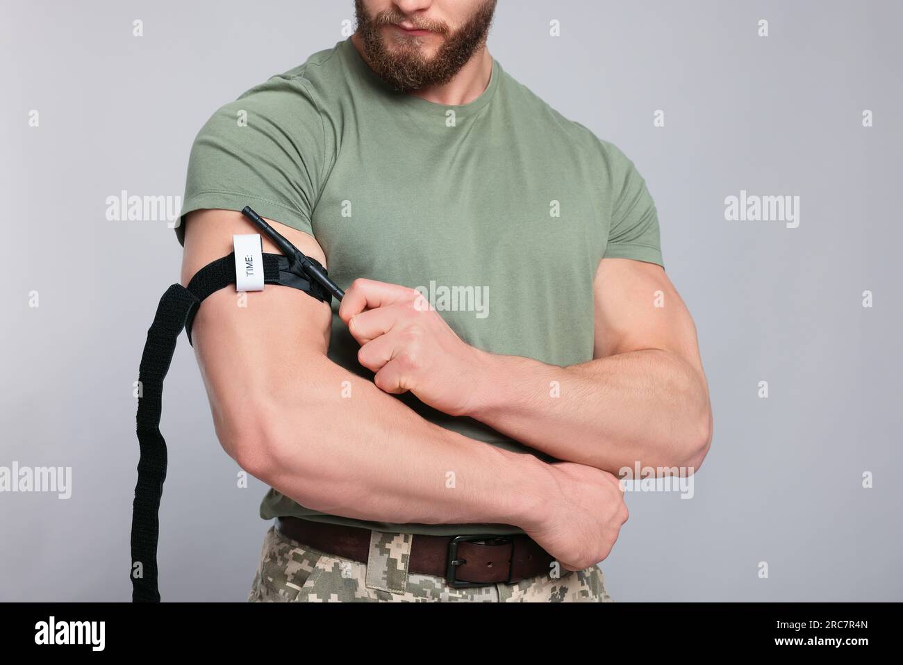 Soldier in military uniform applying medical tourniquet on arm against ...
