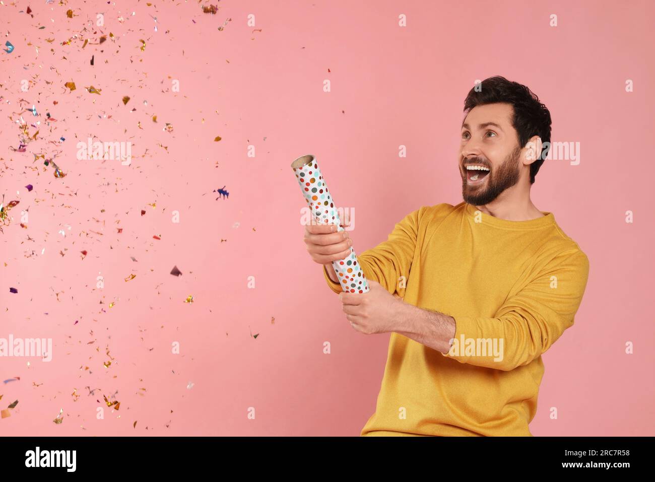 Emotional man blowing up party popper on pink background. Space for ...