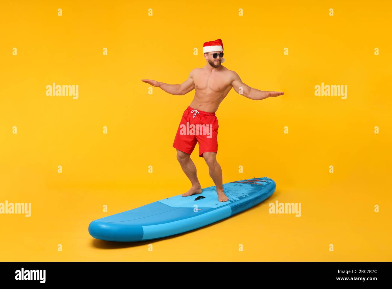 Happy man in Santa hat balancing on SUP board against orange background ...