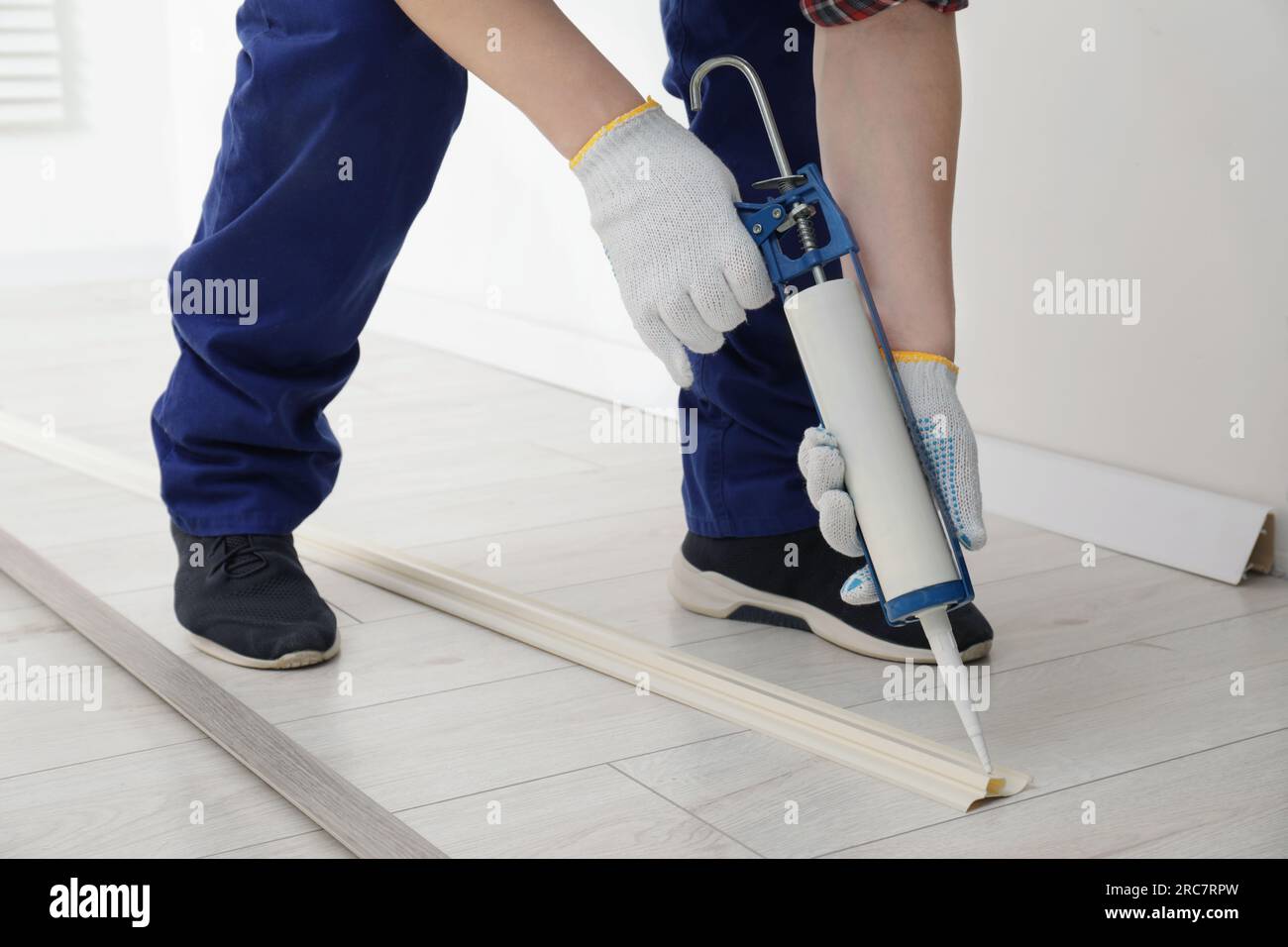 Man using caulking gun while installing plinth on laminated floor in ...