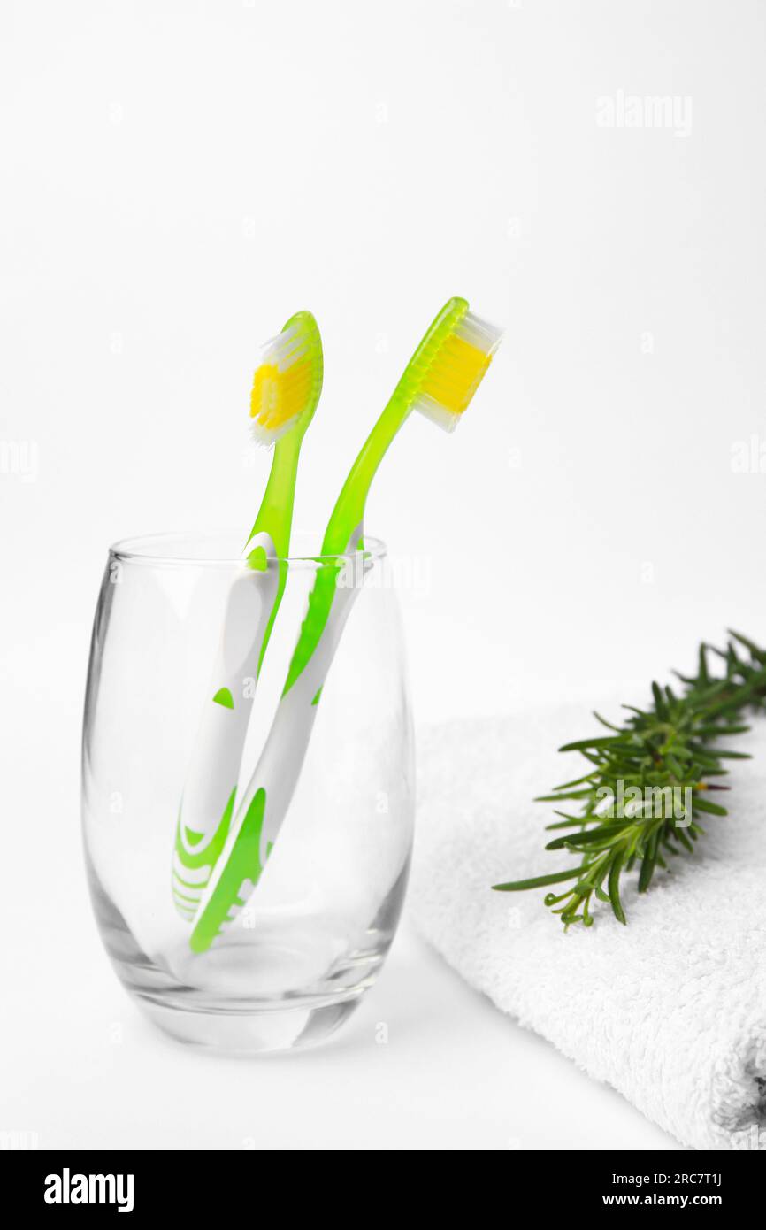 Light green toothbrushes in glass holder, terry towel and rosemary on ...