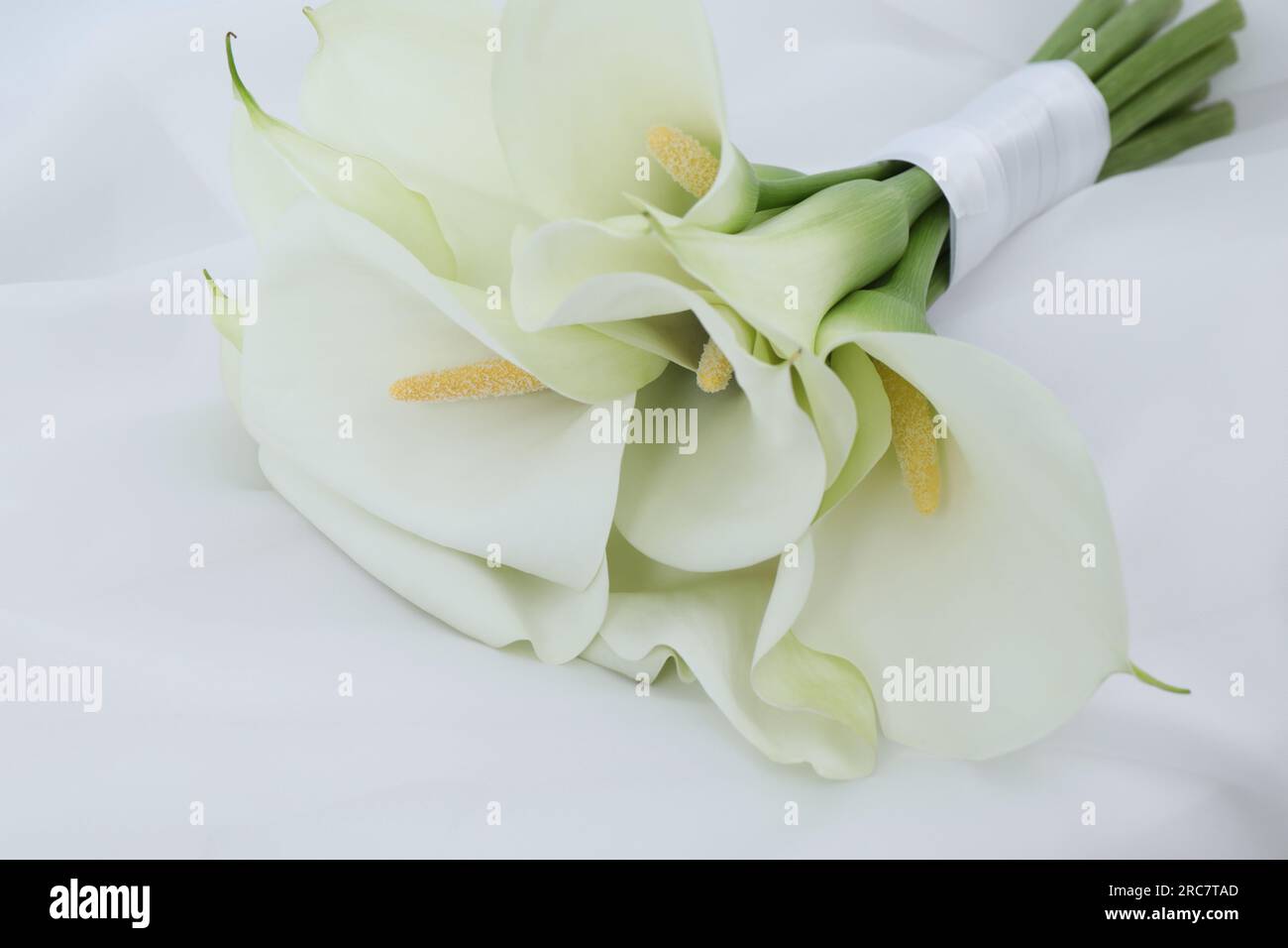 Beautiful calla lily flowers tied with ribbon on white fabric, closeup ...